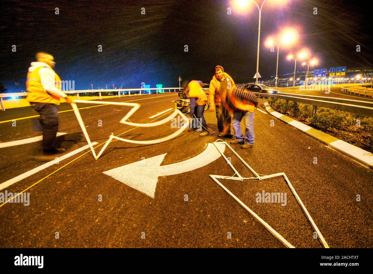 Painting road markings. Workers painting arrows on a road at night ...