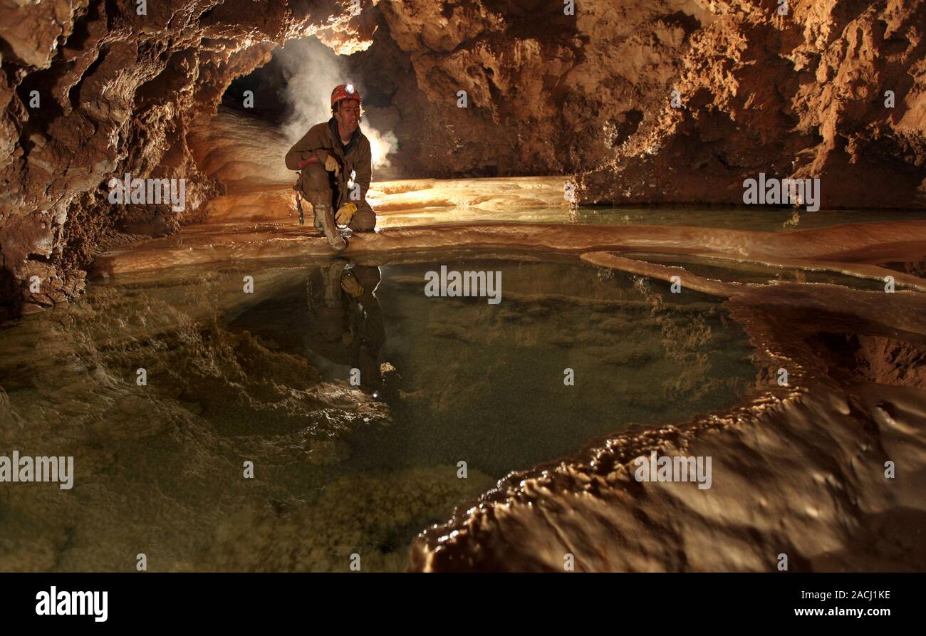 Cave pool. Cave explorer crouching next to the crystal-clear waters of ...