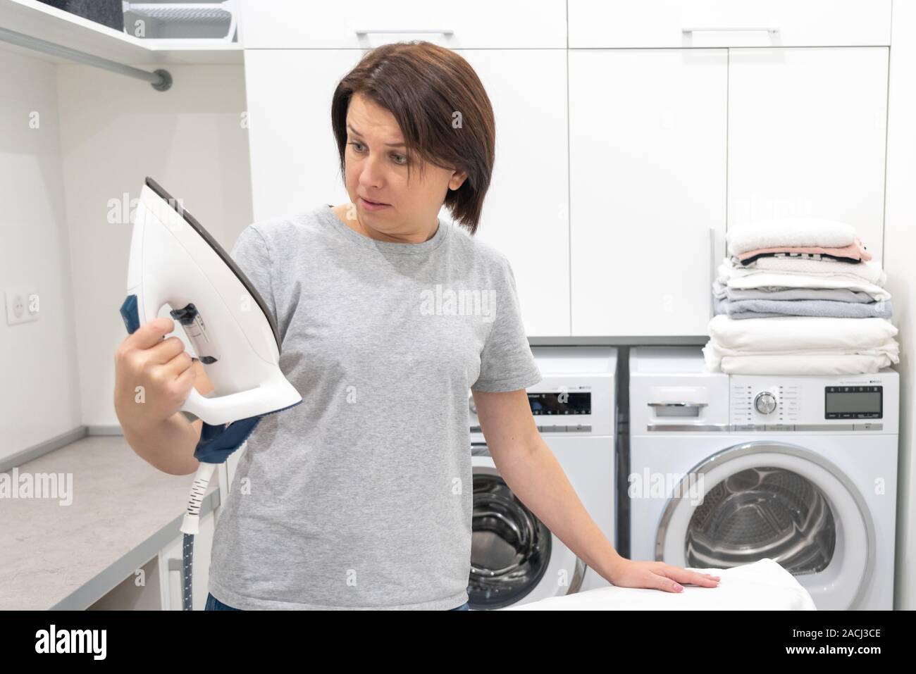 Woman ironing white shirt on board in laundry room with washing machine ...