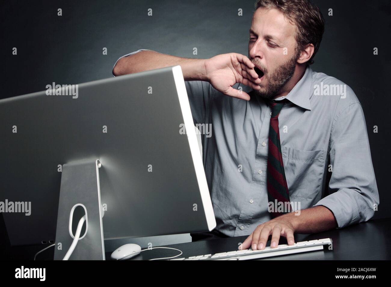 Tiredness at work. Man yawning whilst working on a computer Stock Photo ...