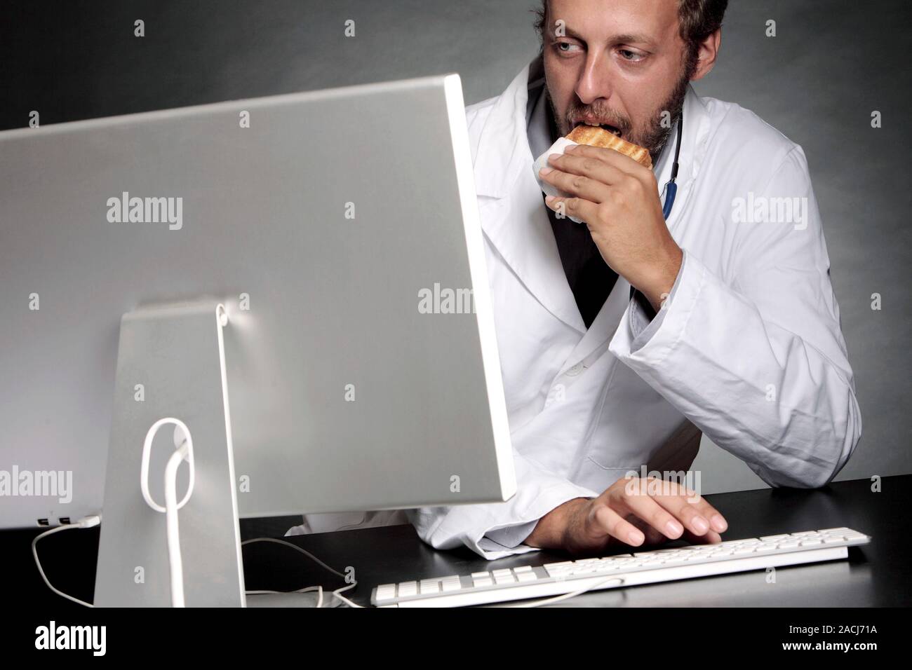 Doctor eating at work whilst using a computer Stock Photo - Alamy