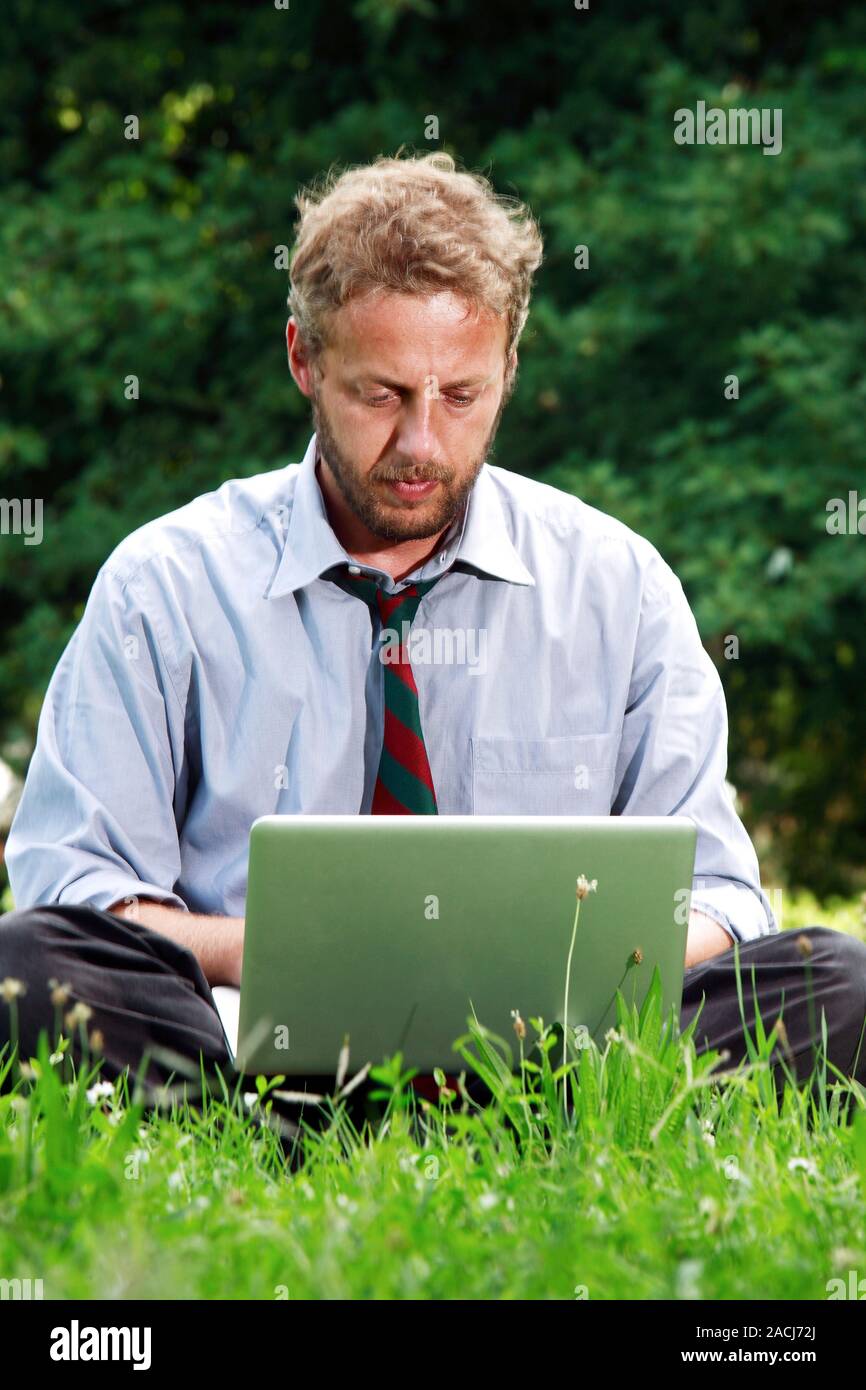 Outdoor working. Man sitting crossed legged on grass working on a ...
