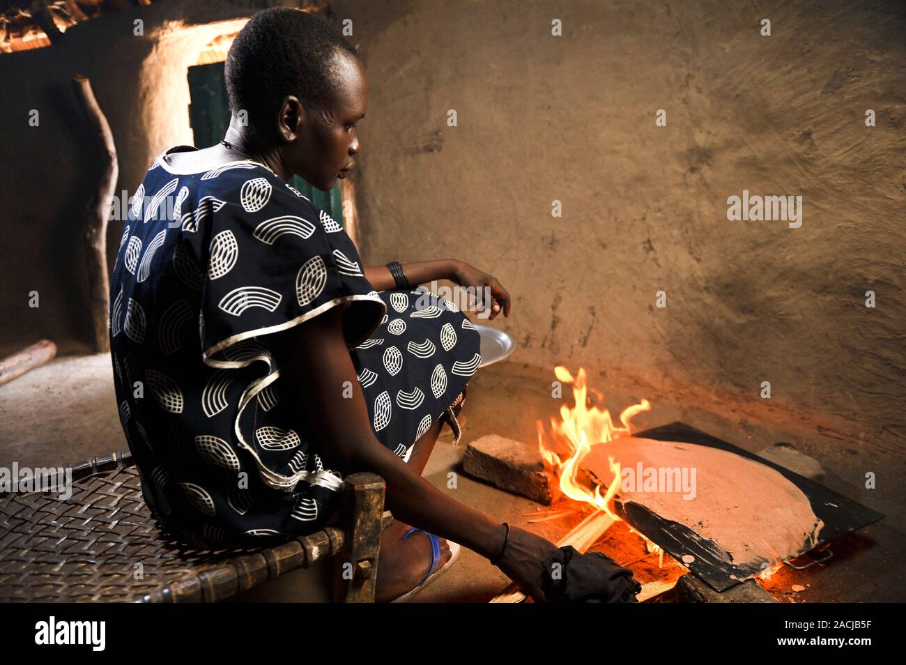 Traditional cooking. Dinka woman cooking on a fire inside a 'tukal', a ...