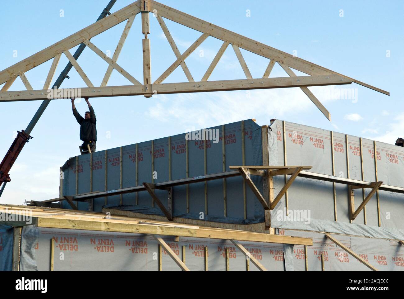 Timber frame house construction. Joiner positioning a roof section of a ...