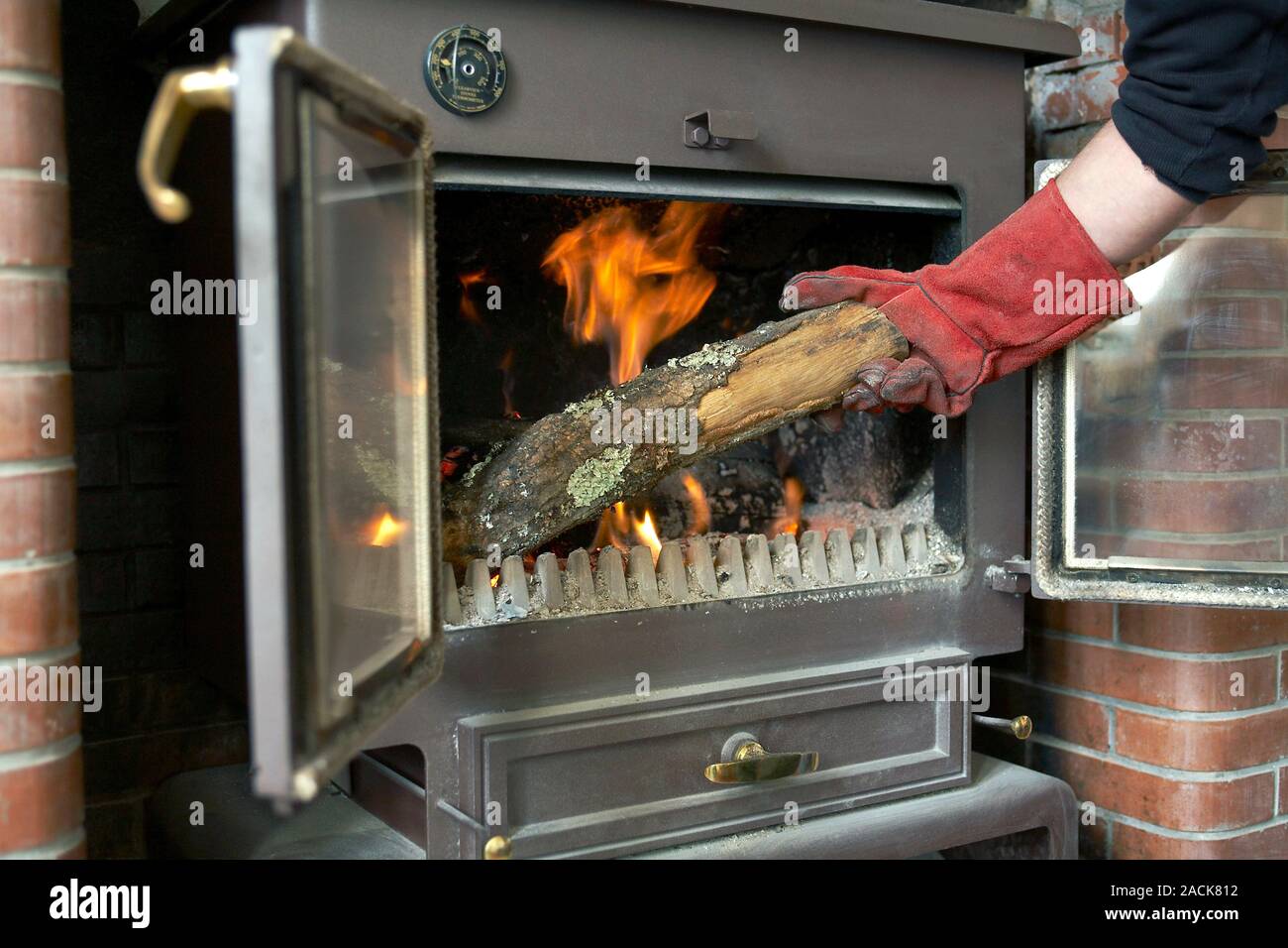 Wood-burning stove. Person placing a log into a domestic wood-burning ...