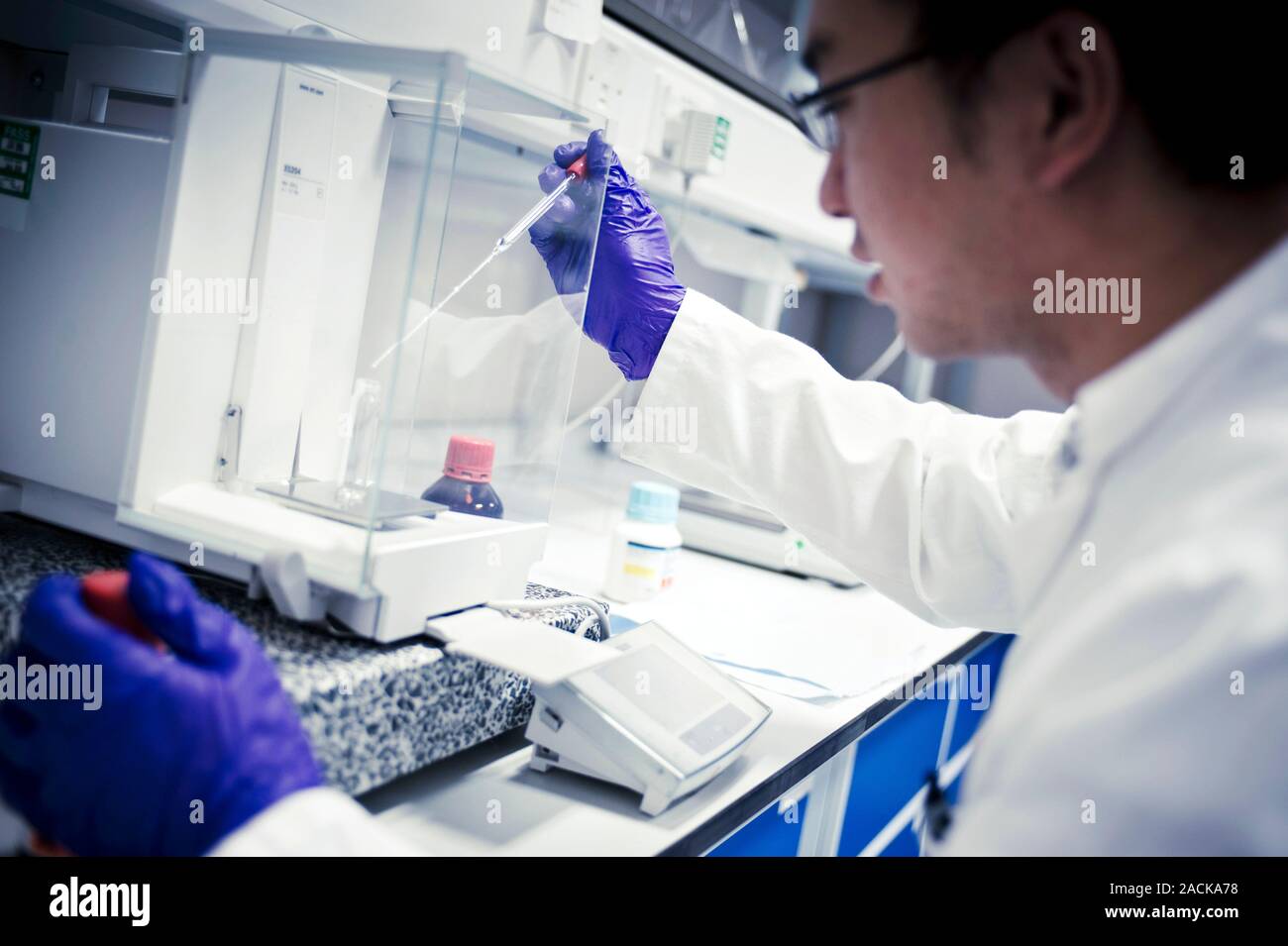 Technician pipetting liquid into a sample bottle for weighing Stock ...