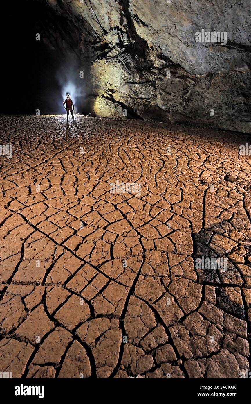 Cave mud floor. Cave explorer examining the cracked mud floor of a ...