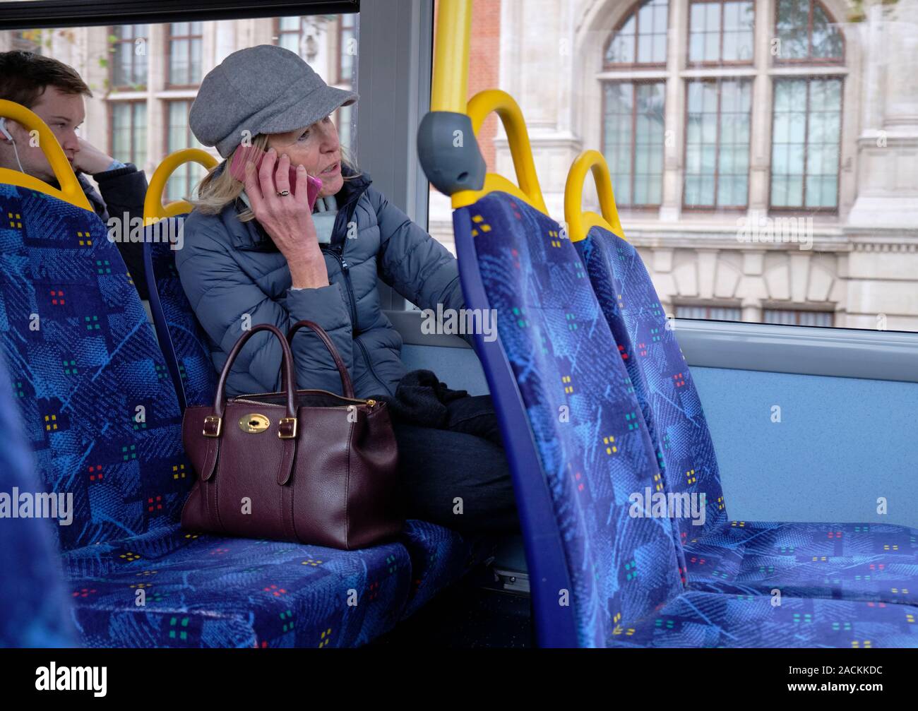 Woman sitting on blue seat on top level of double decker bus speaking ...
