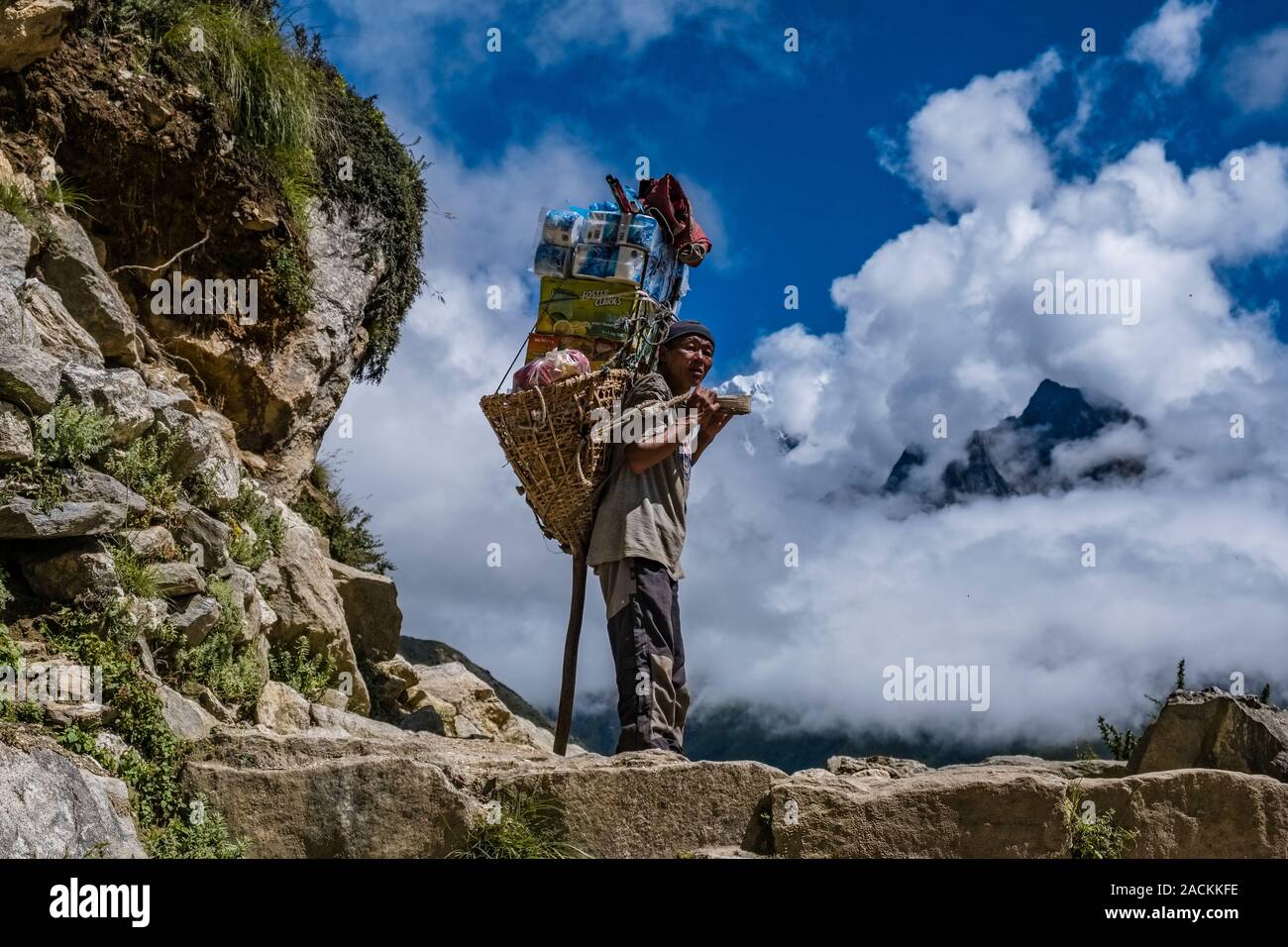 A porter is carrying heavy loads up a steep mountain path Stock Photo ...