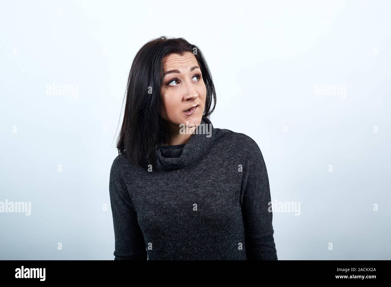 Confused young woman in fashion black sweater biting lip, looking ...