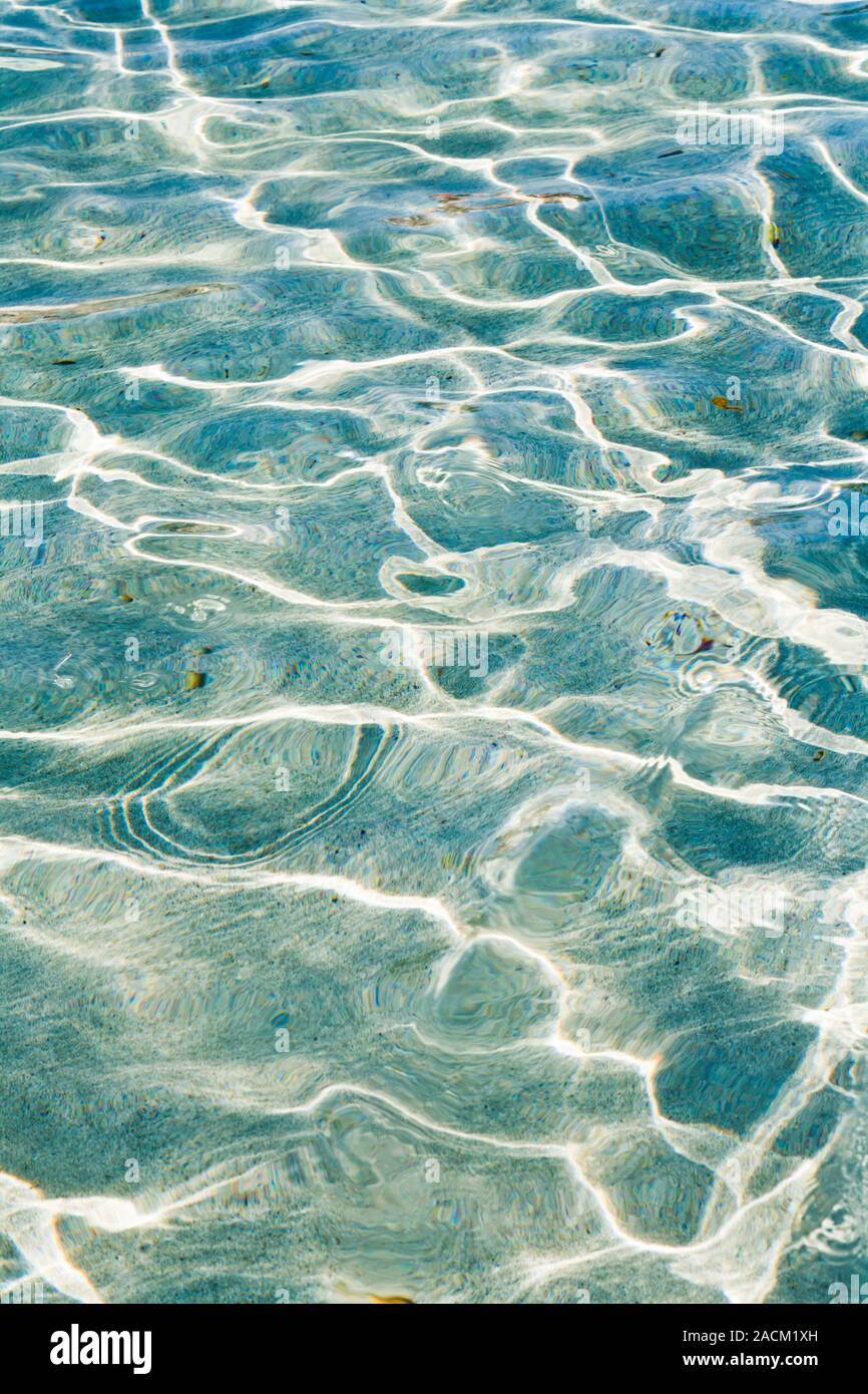 Dappled water, with sunlight reflecting from the surface and the sandy ...