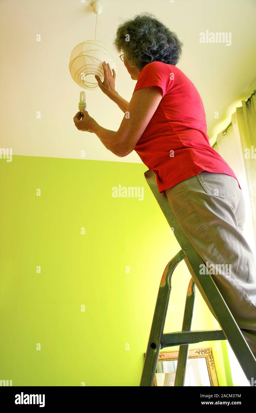 Changing a light bulb. Woman using a step-ladder while changing a light ...