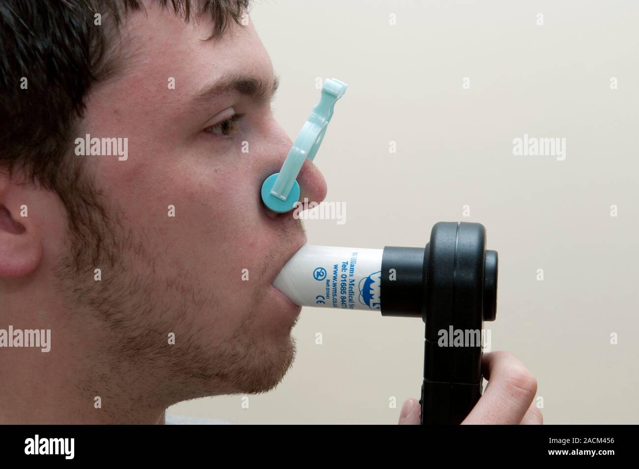 Peak flow meter. Man using a peak flow meter (spirometer) to measure ...