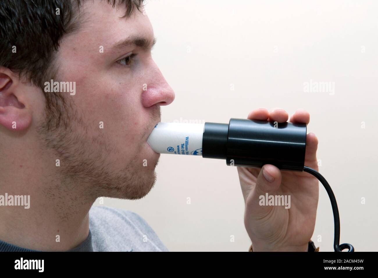 Peak flow meter. Man using a peak flow meter (spirometer) to measure ...