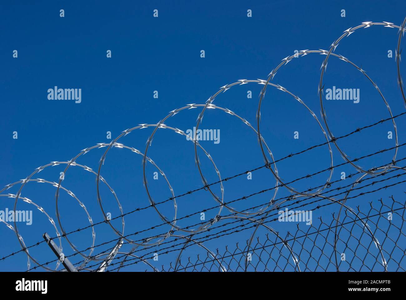 Security fence, topped with razor wire, surrounding industrial premises ...