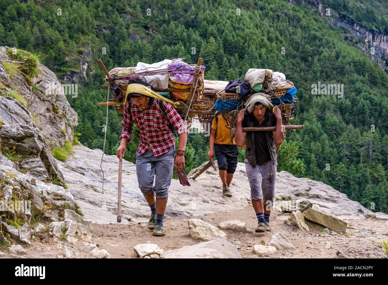 Porters carrying heavy loads up a steep path, goods will be for sale at ...