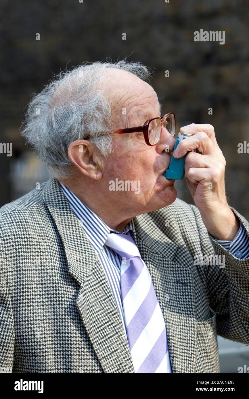 Asthma inhaler use. Elderly man using an inhaler to treat an asthma ...