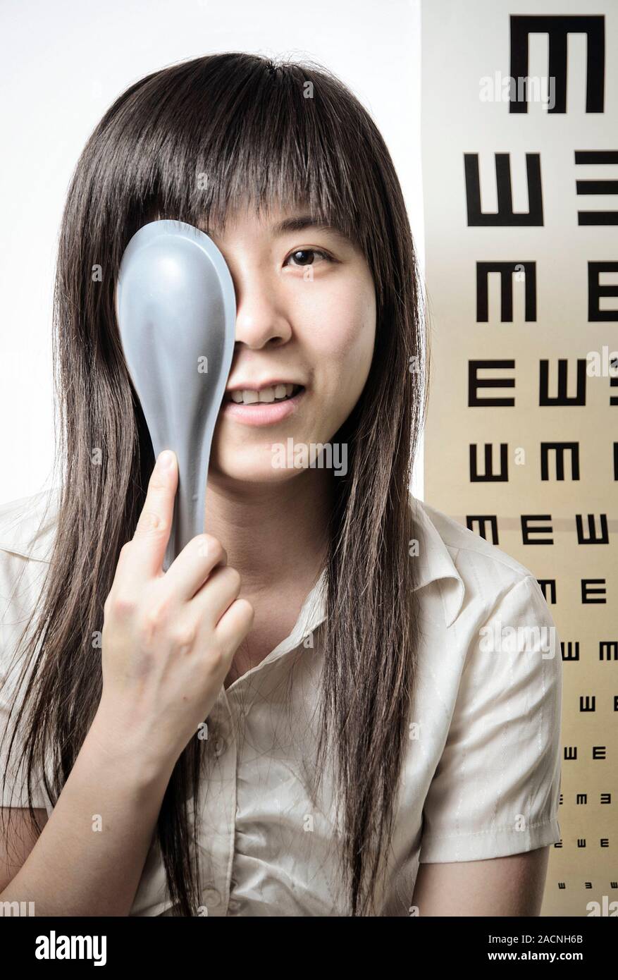 Eye test. Woman reading an eye chart with one eye covered, as part of a ...