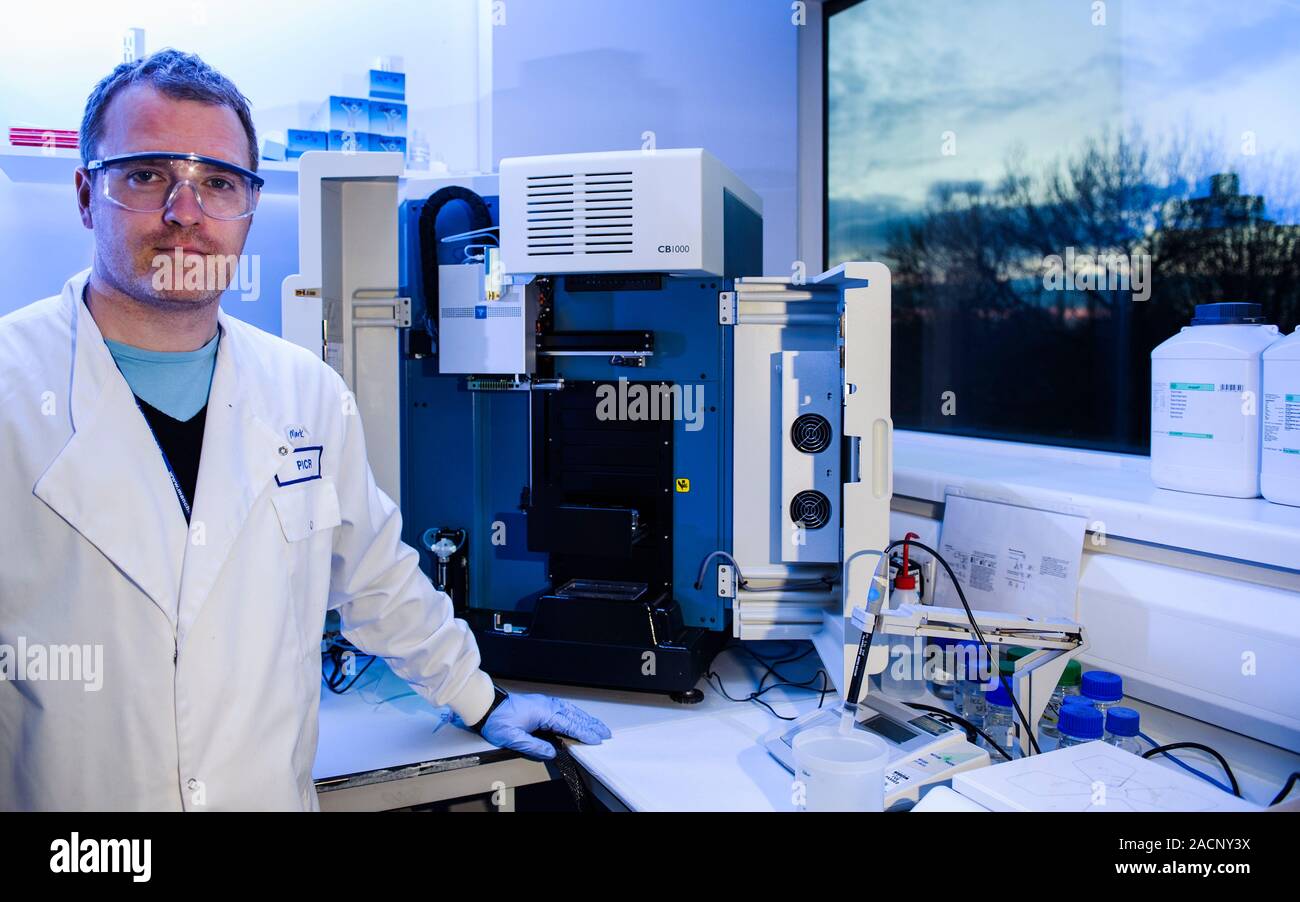 Cancer research. Researcher standing in front of an immunoassay machine ...
