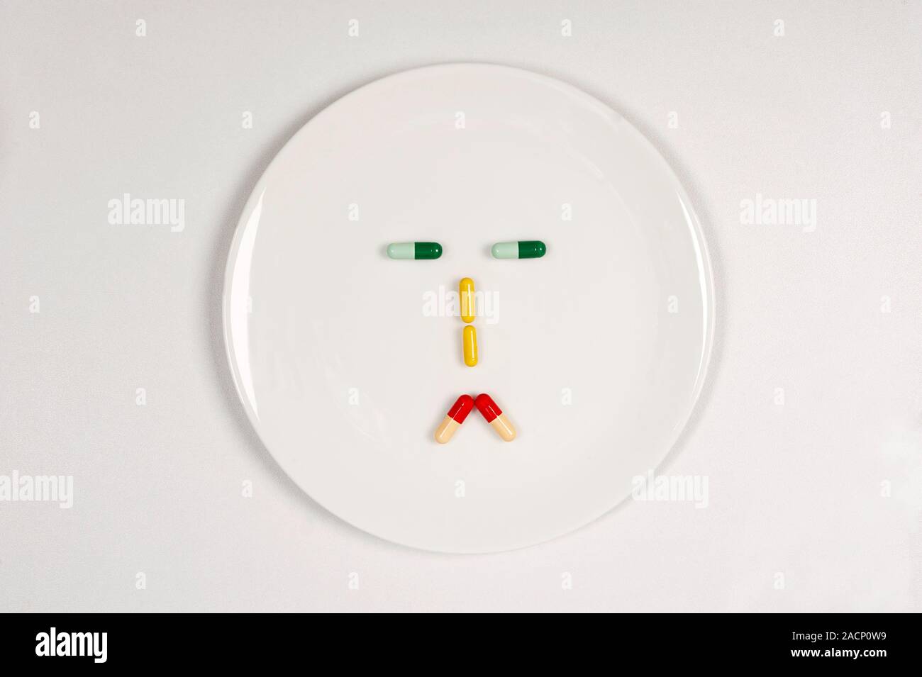 Sad pill face. Drug capsules arranged on a plate to represent a sad ...