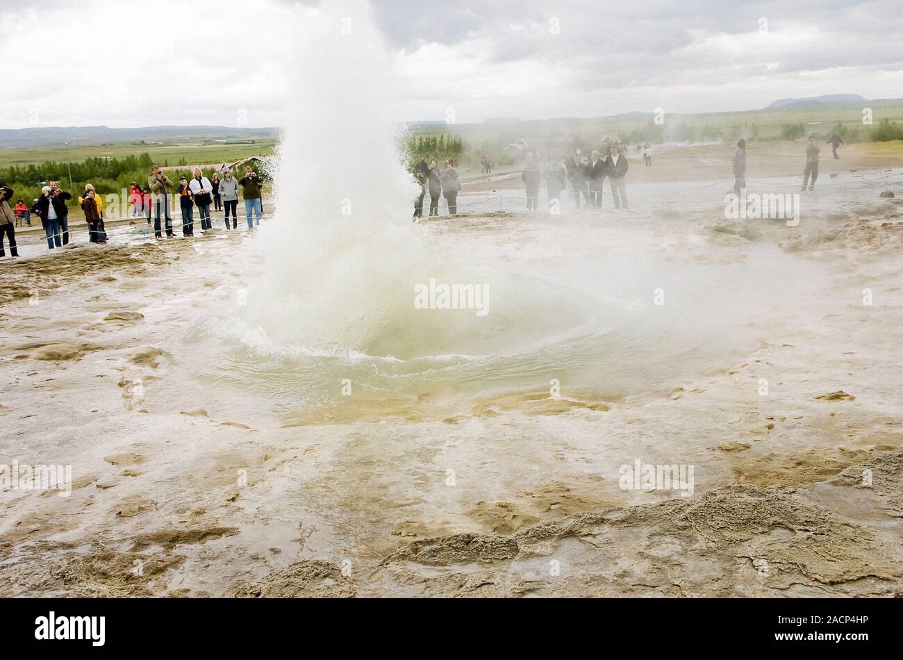 Strokkur Geyser erupting next to tourists. A geyser is a deep natural ...