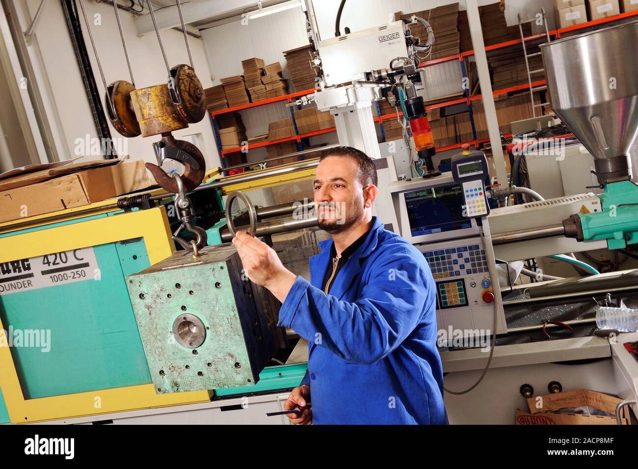 Injection moulding. Worker holding part of an injection mould used to ...