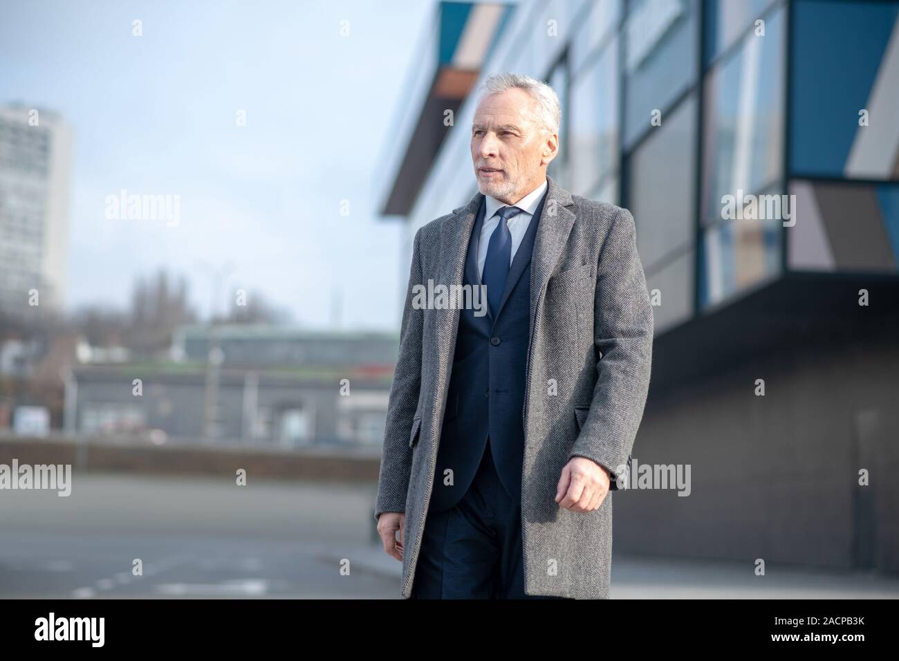 Grey-haired man wearing a grey coat standing near the office Stock ...