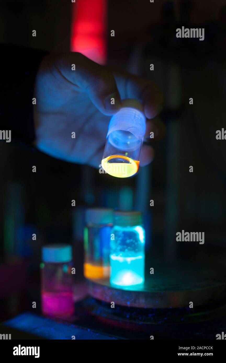 Fluorescent imaging fluids. Lab worker holding a vial containing a ...