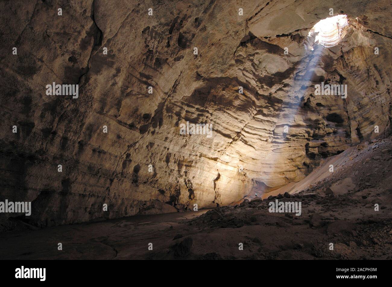 Majlis al Jinn cave. Caver standing in a shaft of sunlight from one of ...