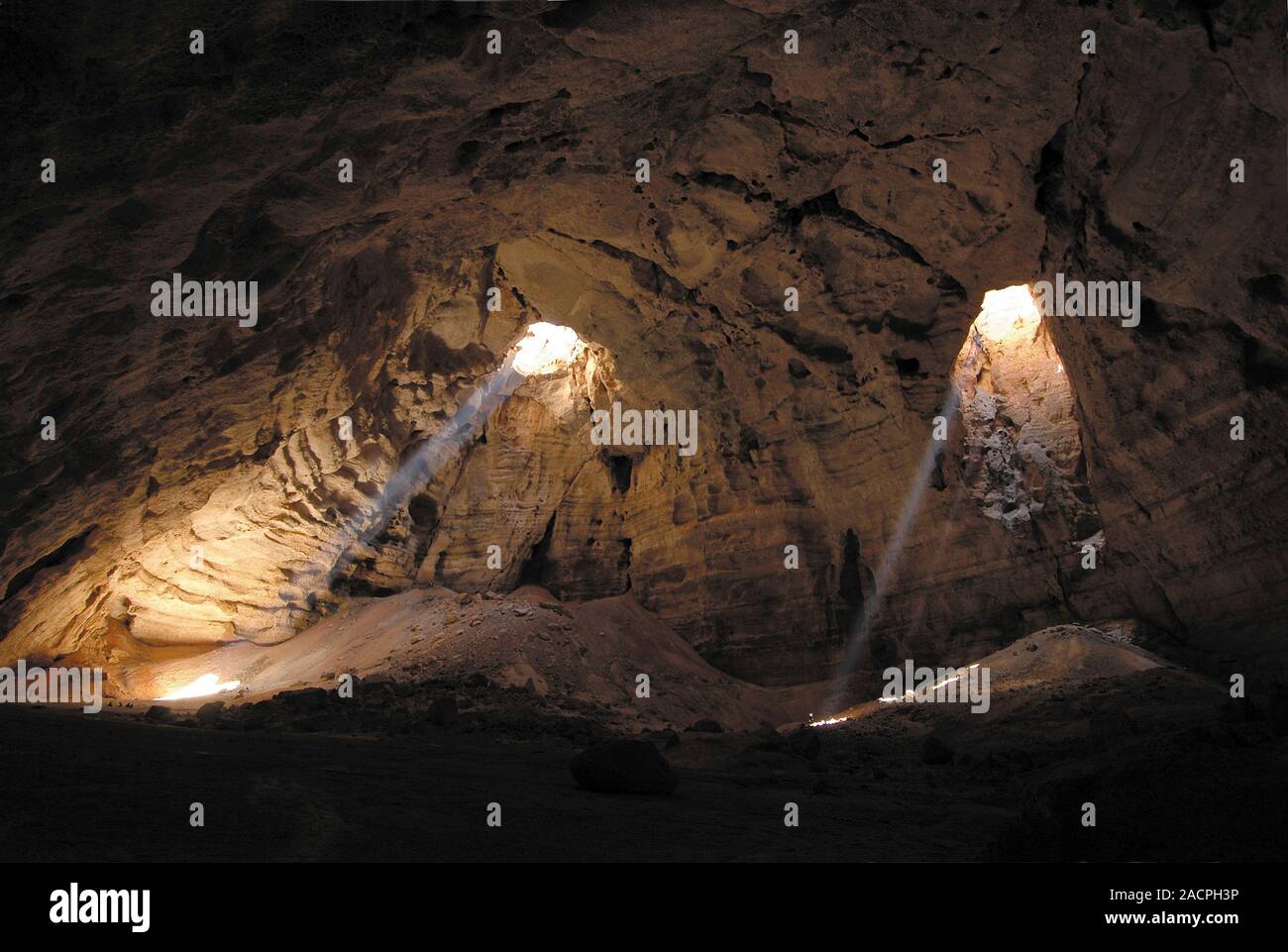 Majlis al Jinn cave. Caver standing in a shaft of sunlight from one of ...