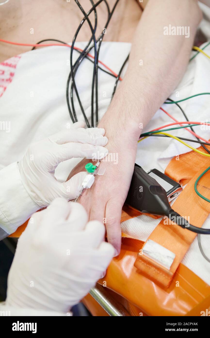 Cardiac patient in an ambulance. Paramedic inserting a cannula into the ...