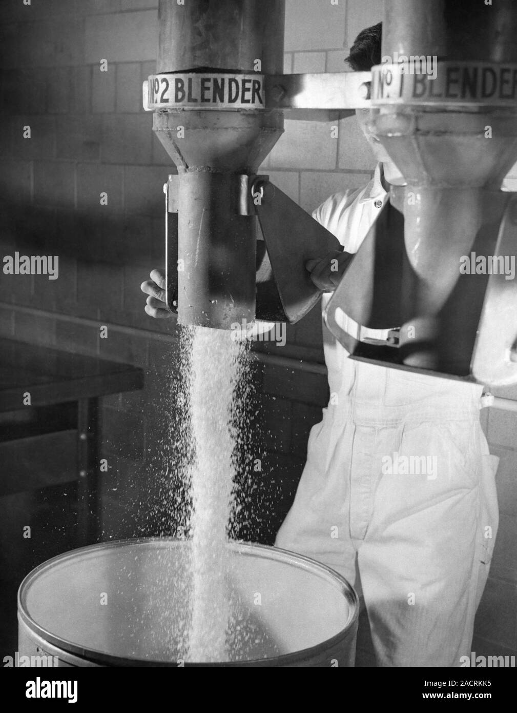 Nylon production. Factory worker directing nylon flakes from a hose ...