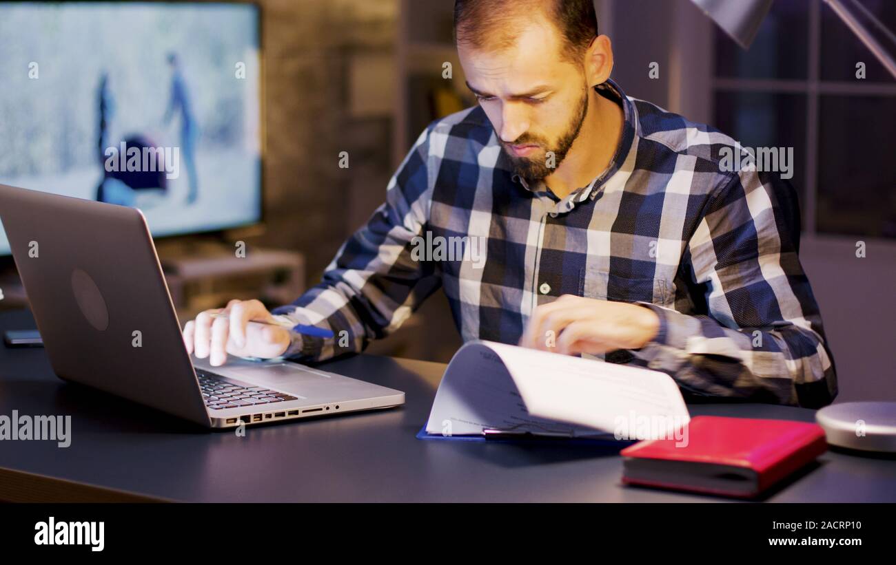 Young entrepreneur working on laptop and signing documents in home ...