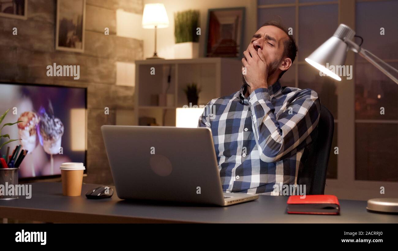 Tired manager yawning while working on laptop in home office during ...