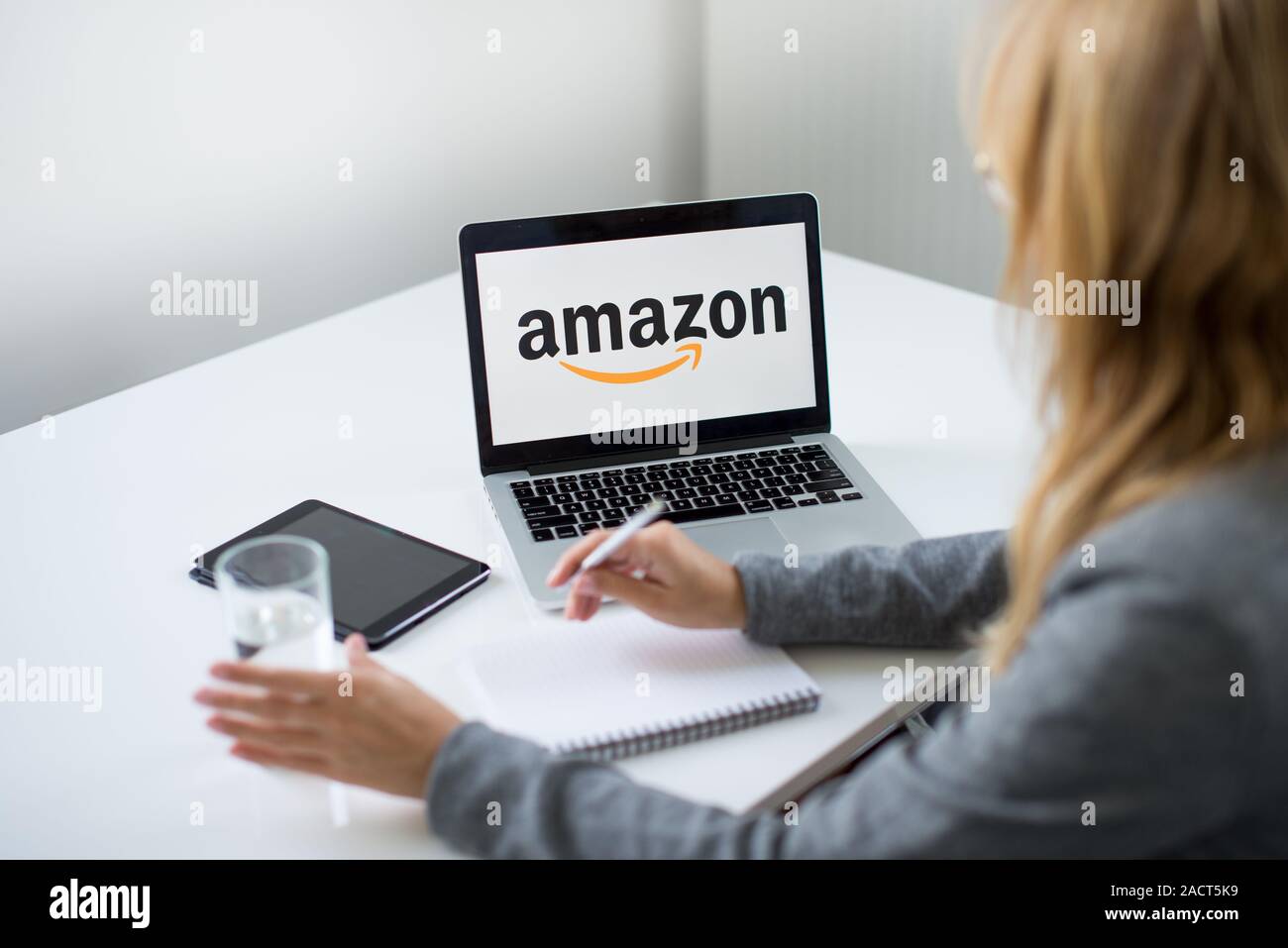 Young woman using laptop with Amazon logo in the screen seeting at the ...