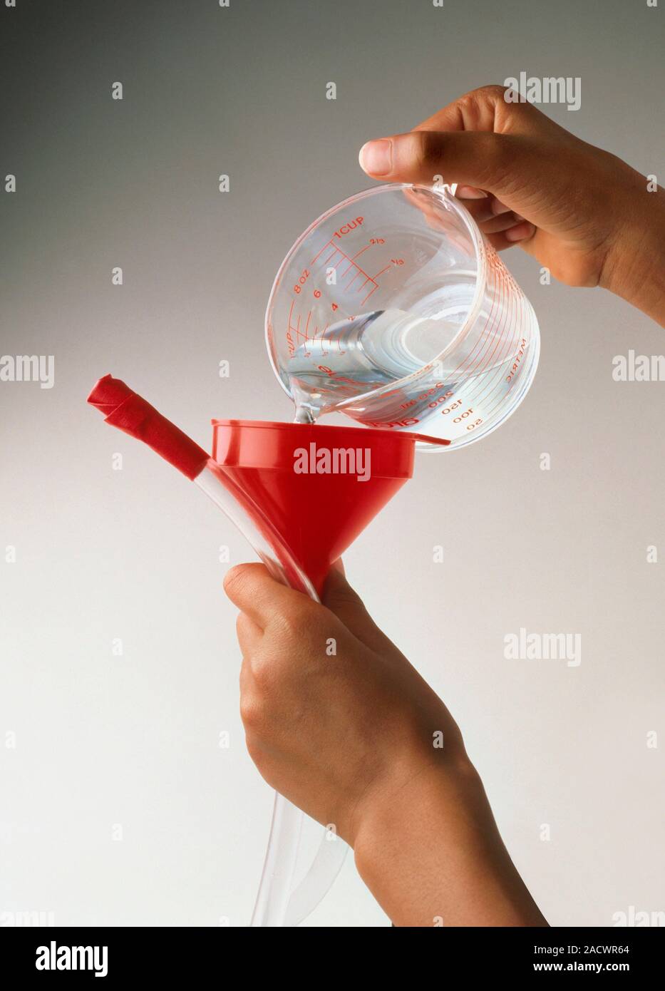 Hand pouring water from jug into funnel connected to tube, close-up ...