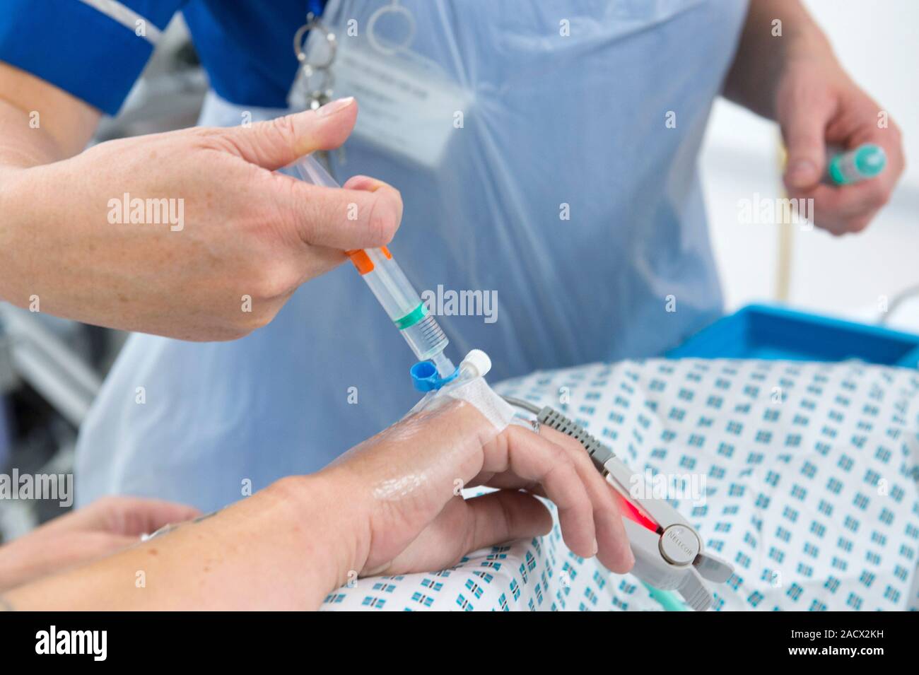 Nurse administering an injection to a patient via a cannula in their ...