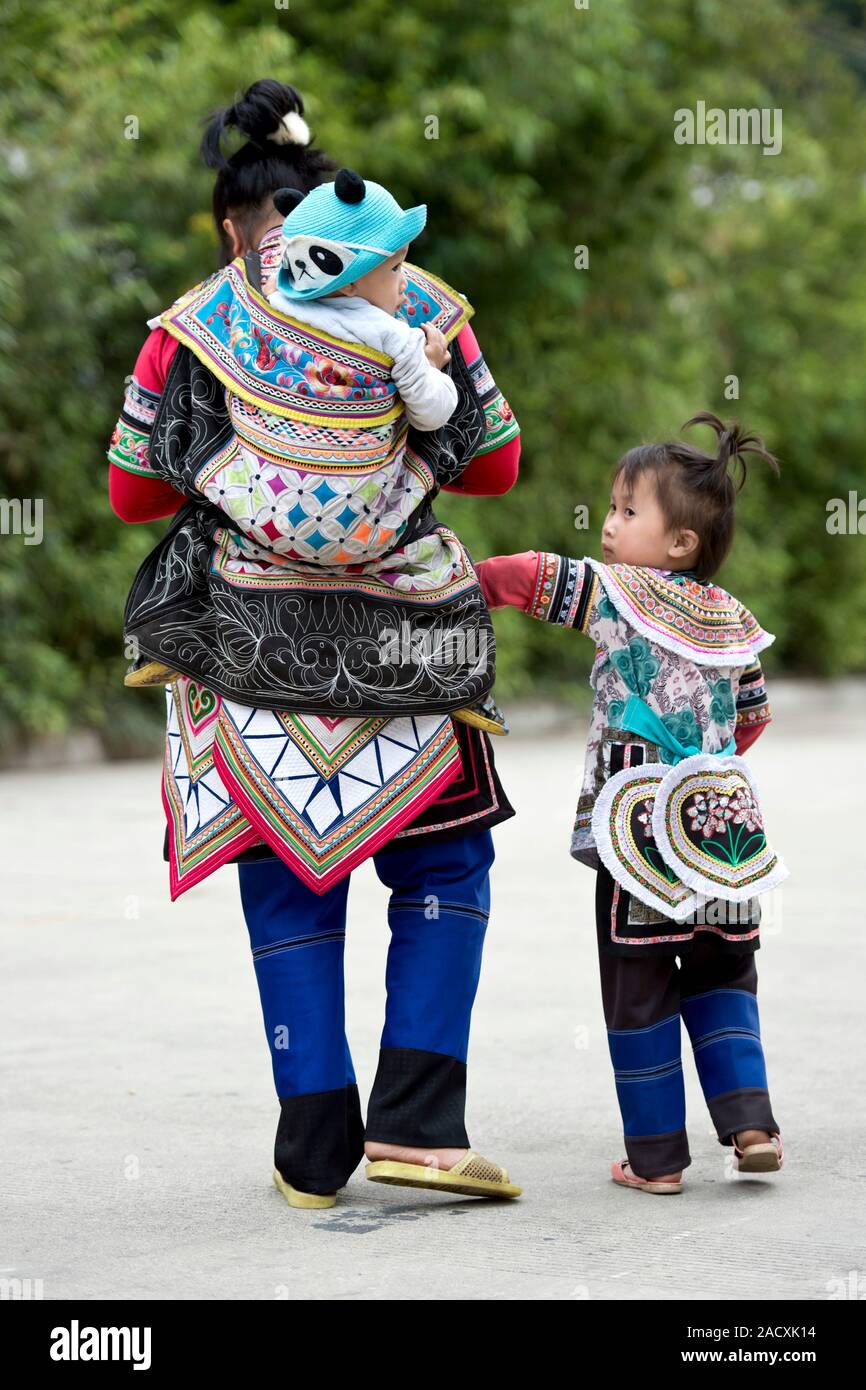 A Yi woman in traditional dress with her daughter and baby on her back ...