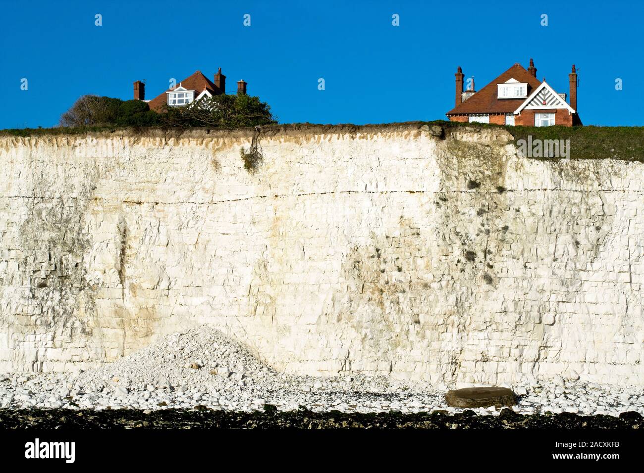 Chalk cliffs and houses above a beach with a pile of fallen chalk at ...