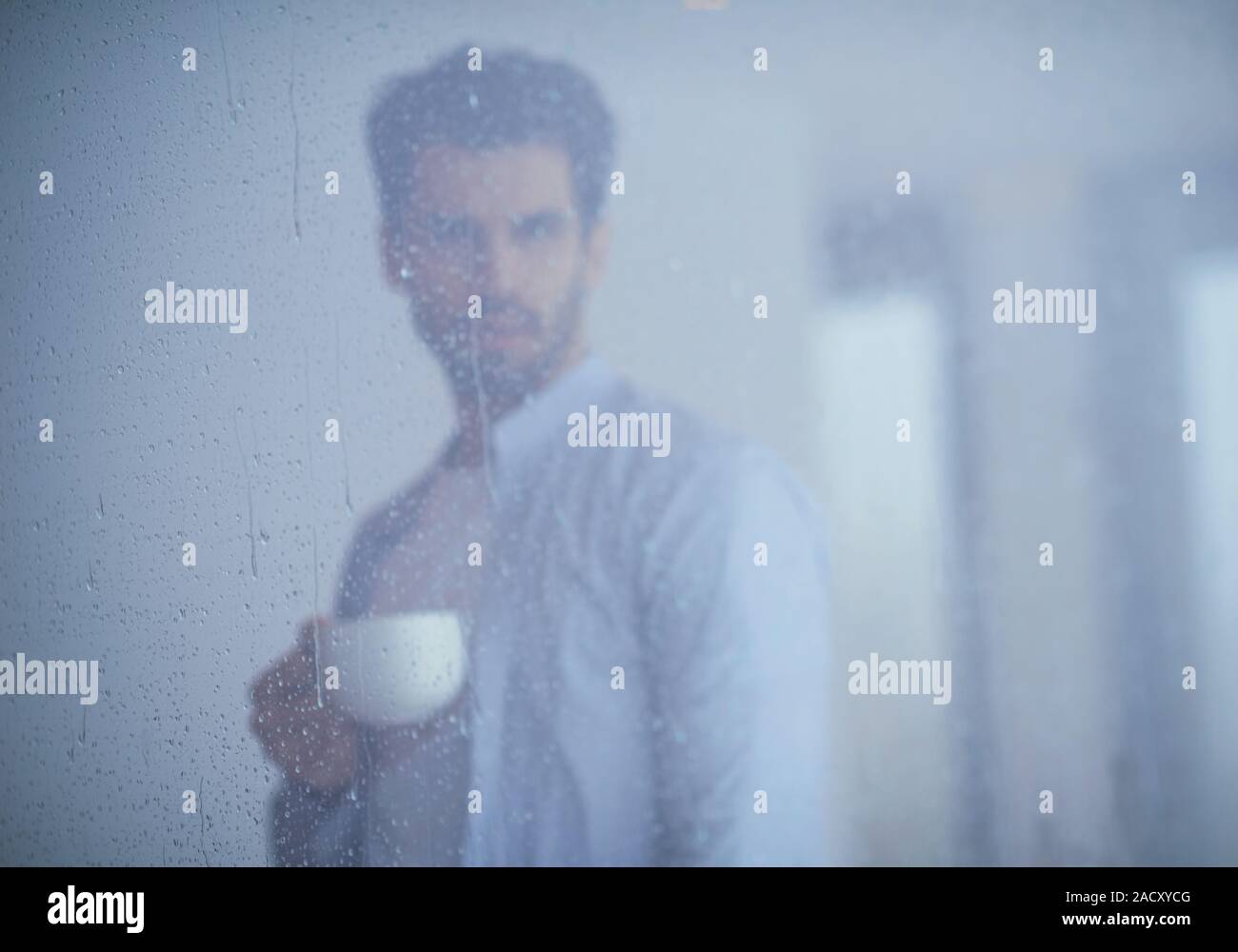 relaxed young man drink first morning coffee withh rain drops on window ...