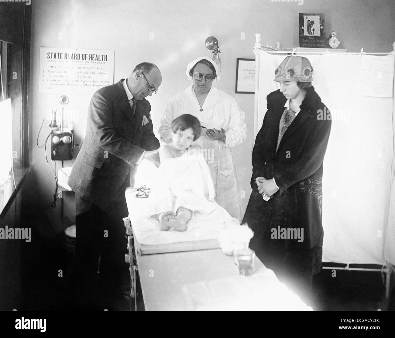 1920s child health checkup. Mother (right) watching as her daughter ...