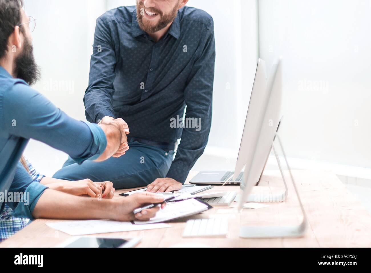 smiling colleagues shaking hands near the desktop Stock Photo - Alamy