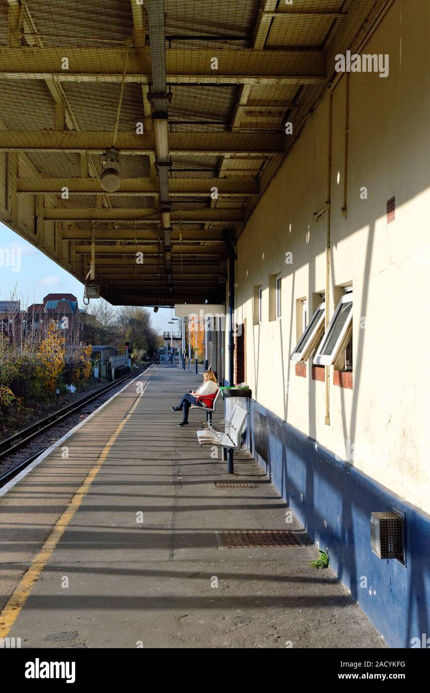 A middle aged woman sitting alone on an empty railway station platform ...