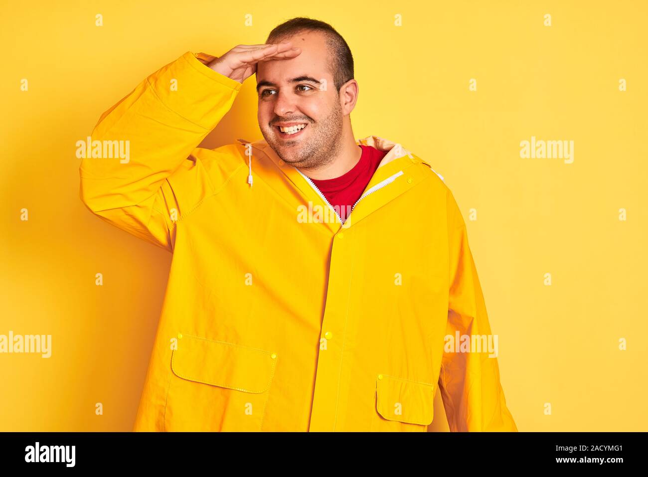 Young man wearing rain coat standing over isolated yellow background ...