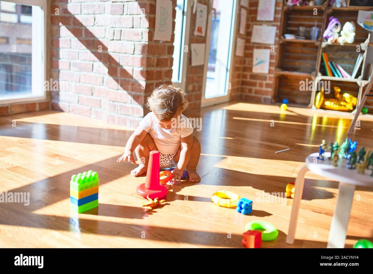 Adorable toddler building pyramid using hoops around lots of toys at ...