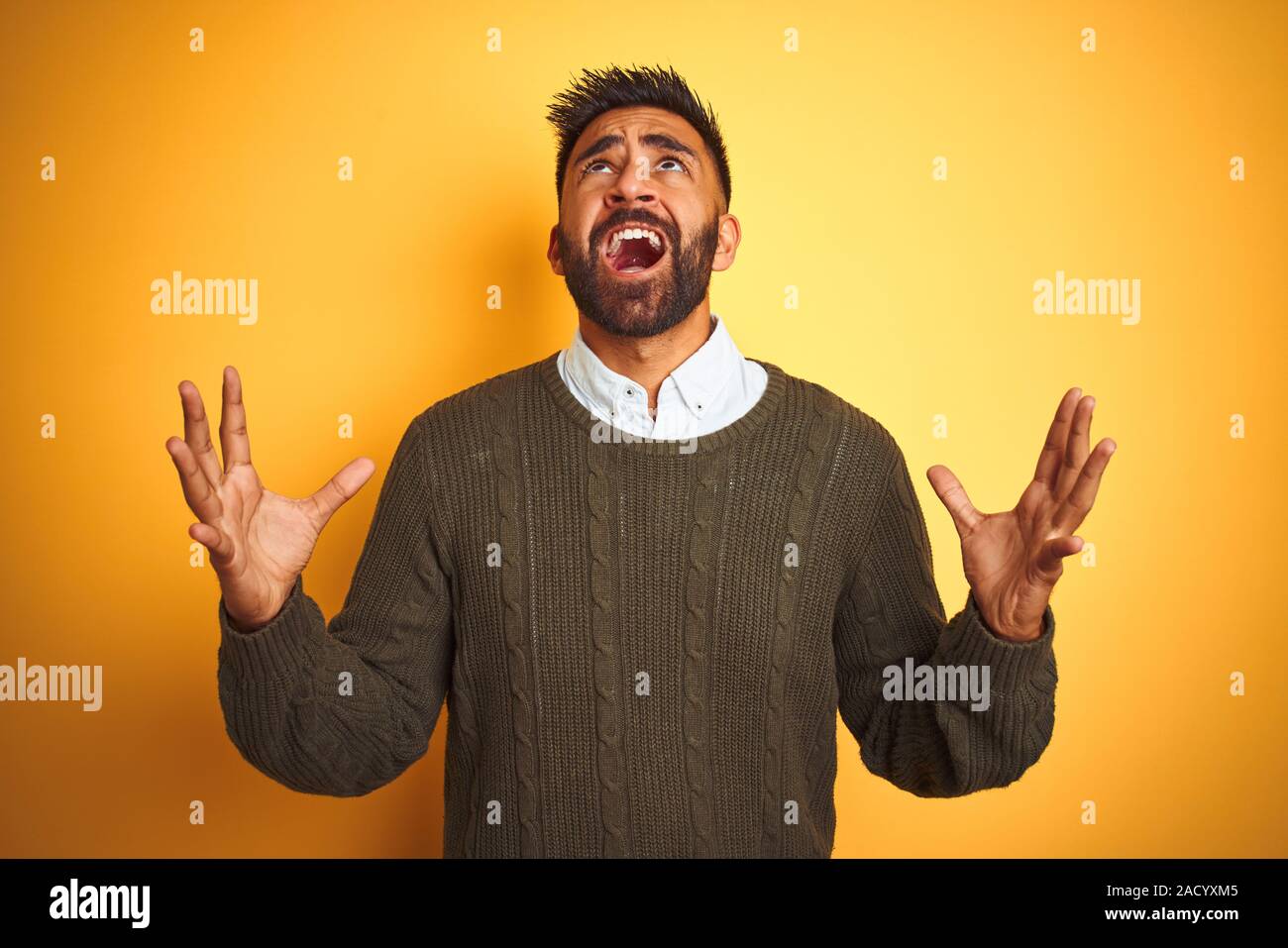Young indian man wearing green sweater and shirt standing over isolated ...