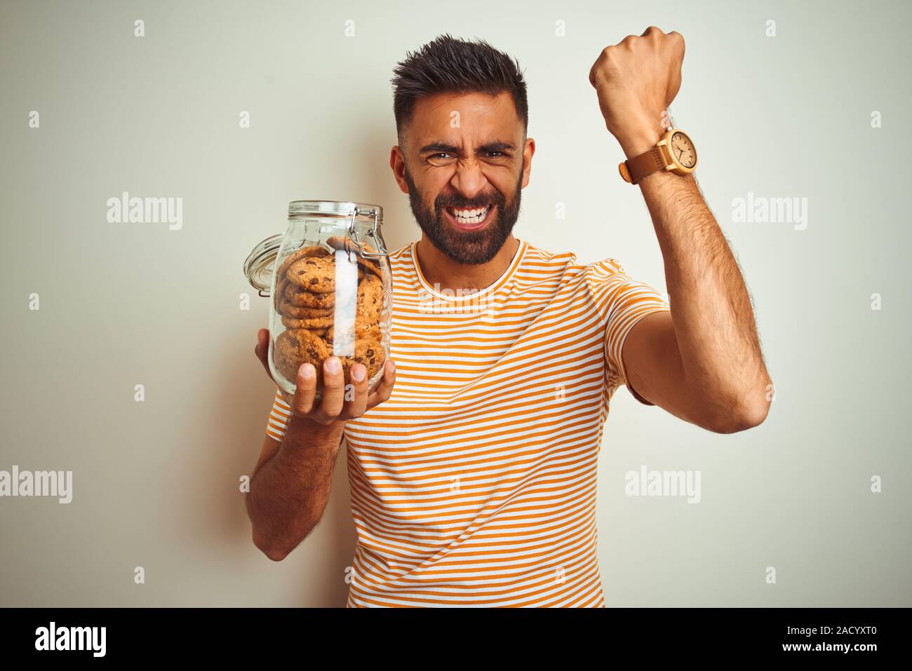Young indian man holding jar of cookies standing over isolated white ...