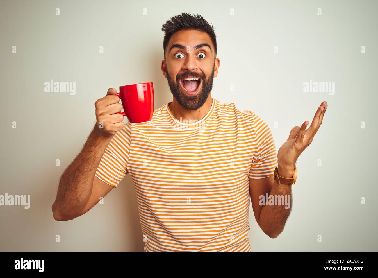 Young indian man drinking red cup of coffee standing over isolated ...
