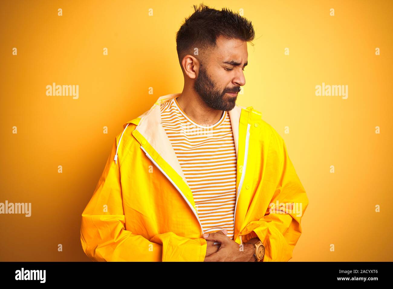 Young indian man wearing raincoat standing over isolated yellow ...