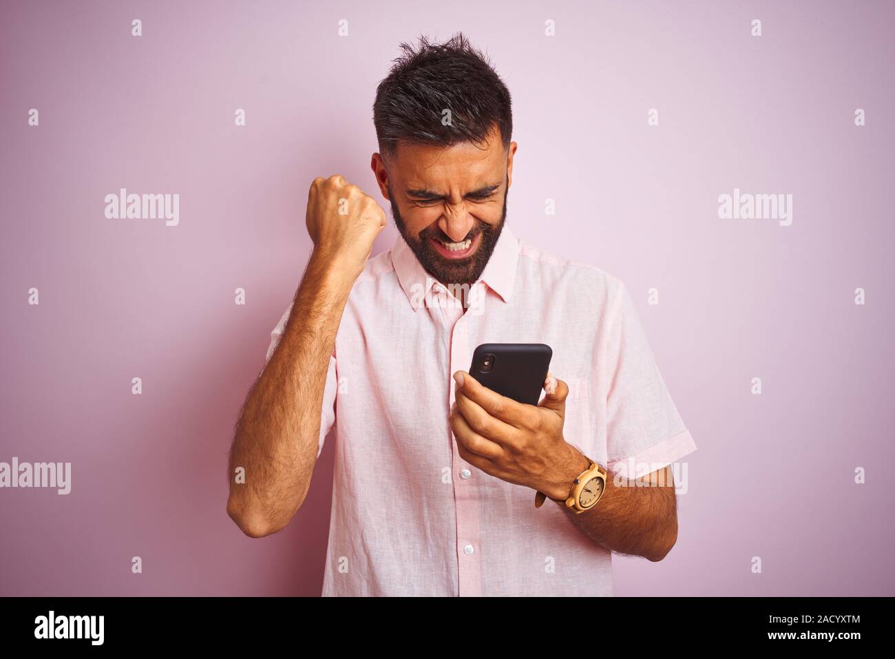 Young indian man using smartphone standing over isolated pink ...